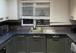 Cozinha equipada com micro-ondas embutido, pia e janela com persianas.