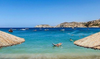 Uma praia com águas azul-claras, barcos e pessoas nadando.