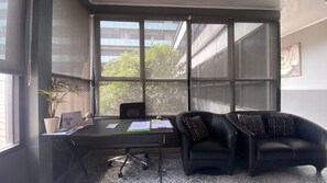 Quarto com escrivaninha, cadeira e amplas janelas.
