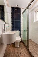 Uma casa de banho moderna com lavatório redondo, sanita e cabine de duche com parede de vidro.