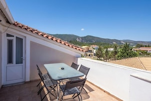 Uma varanda com mesa e cadeiras, com vista para uma paisagem montanhosa.
