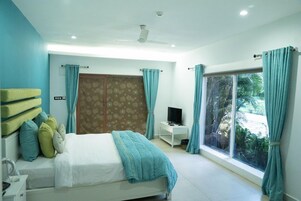 Quarto com cama, televisão, escrivaninha e janela com cortinas.