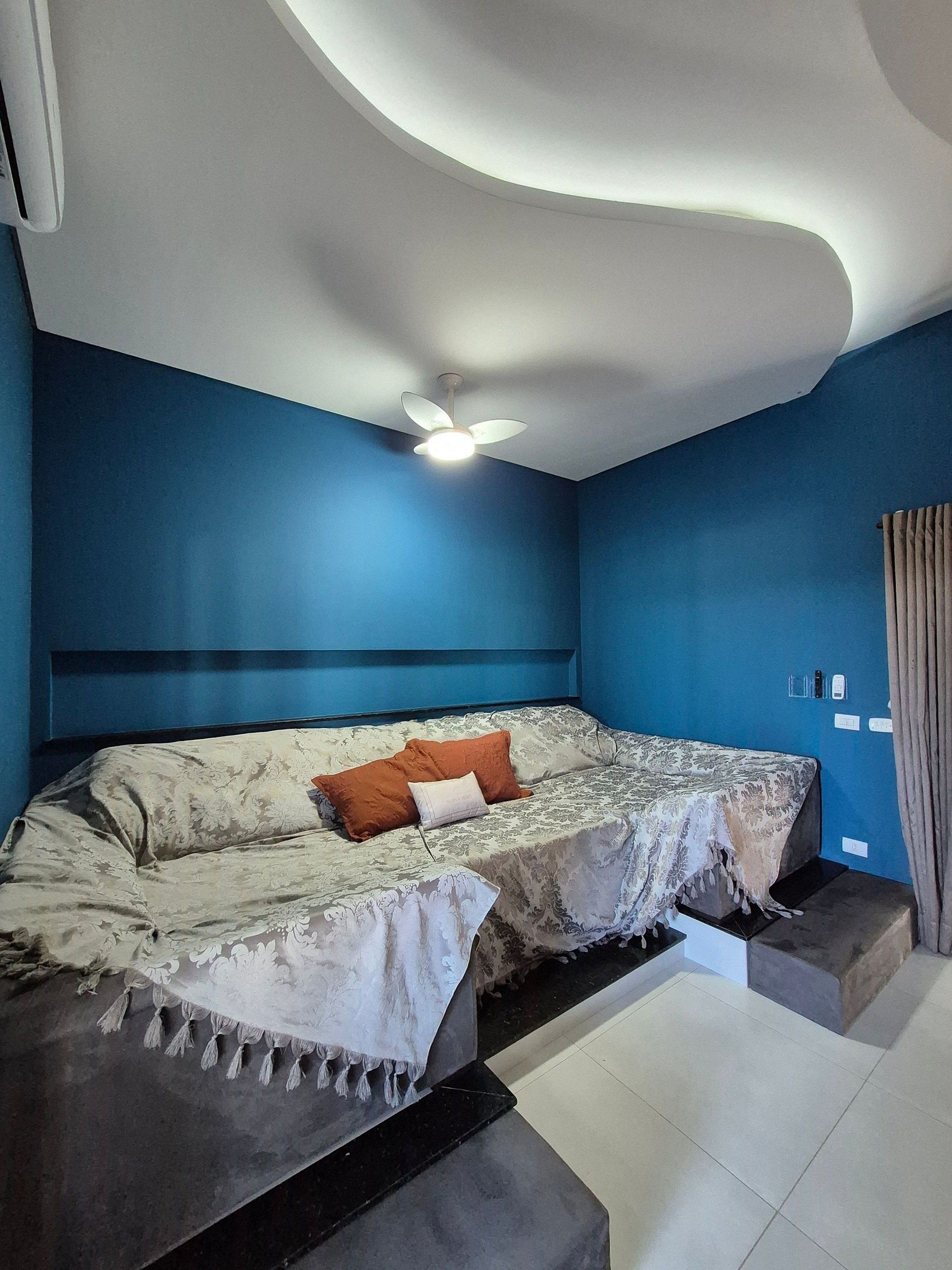 Quarto com cama, ventilador de teto e parede azul.