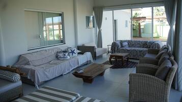 Ampla sala de estar com sofá, poltronas, mesa de centro e uma grande porta de vidro deslizante que dá para um pátio externo.