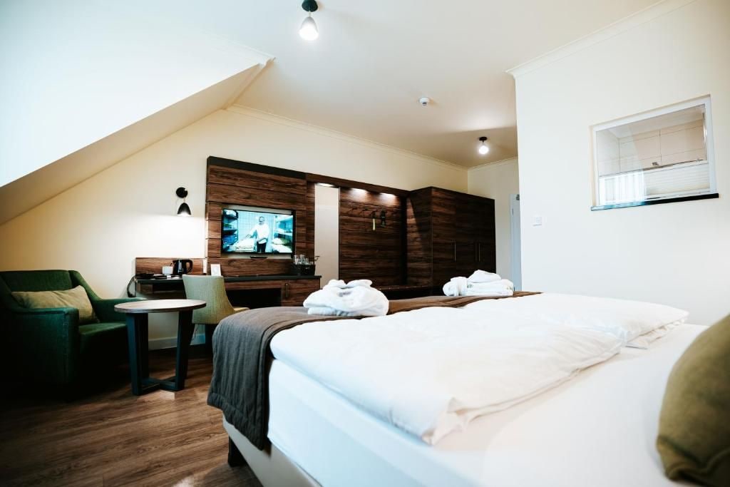 Quarto de hotel com cama, escrivaninha, cadeira, televisão e parede de destaque em madeira.
