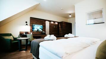 Quarto de hotel com cama, escrivaninha, cadeira, televisão e parede de destaque em madeira.
