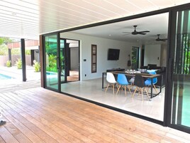 Uma área de refeições moderna com porta de vidro que dá para um espaço ao ar livre, ventilador de teto e TV de tela plana.