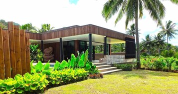 Uma casa moderna com área externa coberta, rodeada por vegetação exuberante e palmeiras.