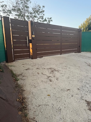 Área cercada por uma grade de metal, chão de concreto e uma parede verde ao fundo.