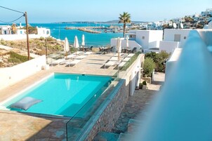 Piscina no terraço com água azul cristalina, rodeada por edifícios brancos e vista para o mar.
