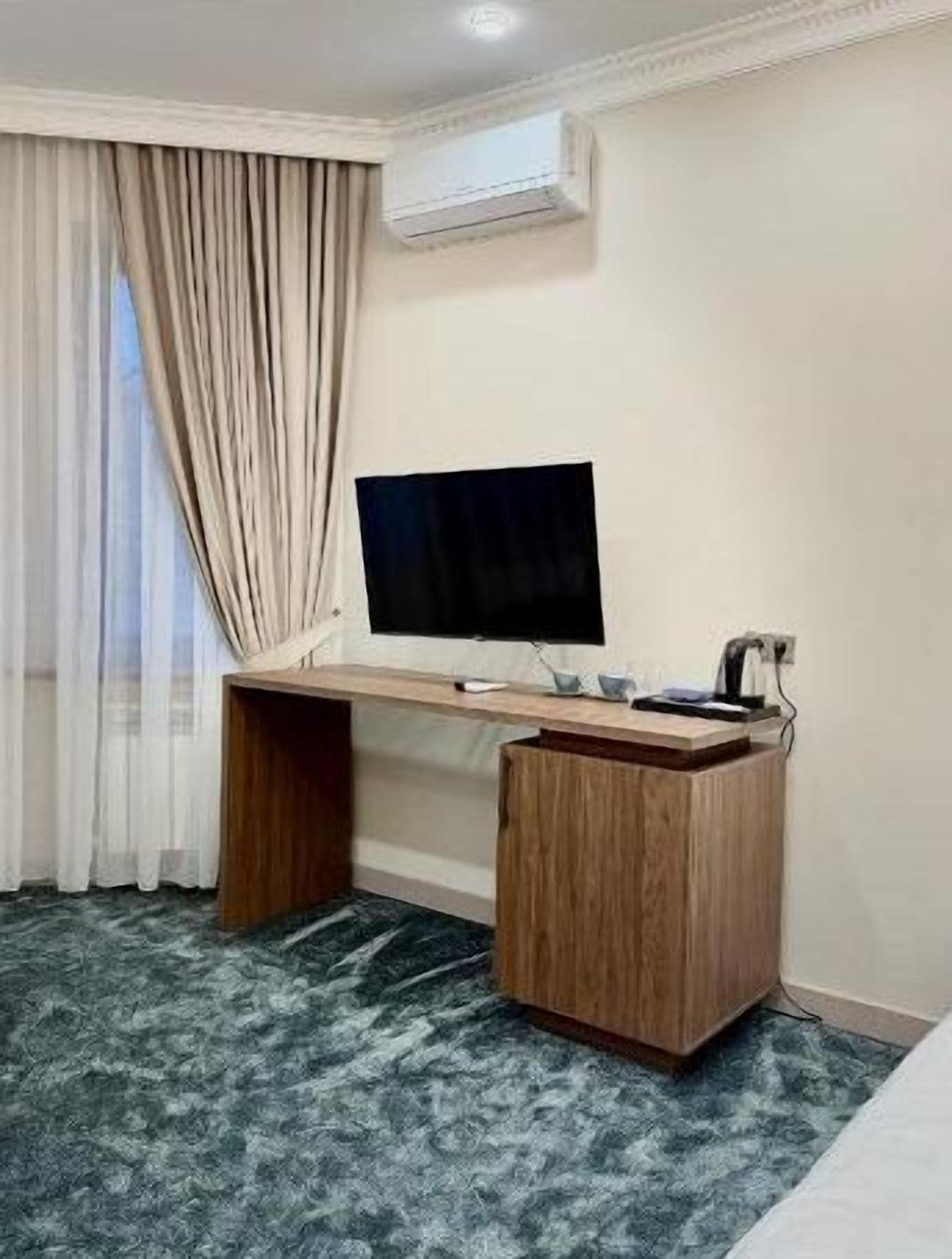 Quarto de hotel com escrivaninha de madeira, televisão de tela plana e um pequeno alto-falante.
