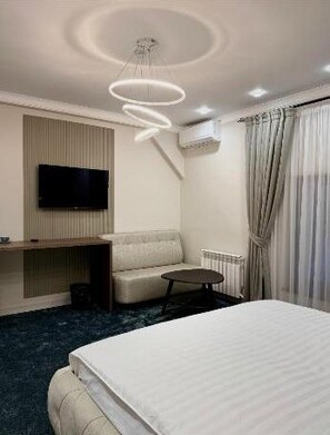 Quarto de hotel com cama, sofá, mesa pequena, televisão e luminária no teto.