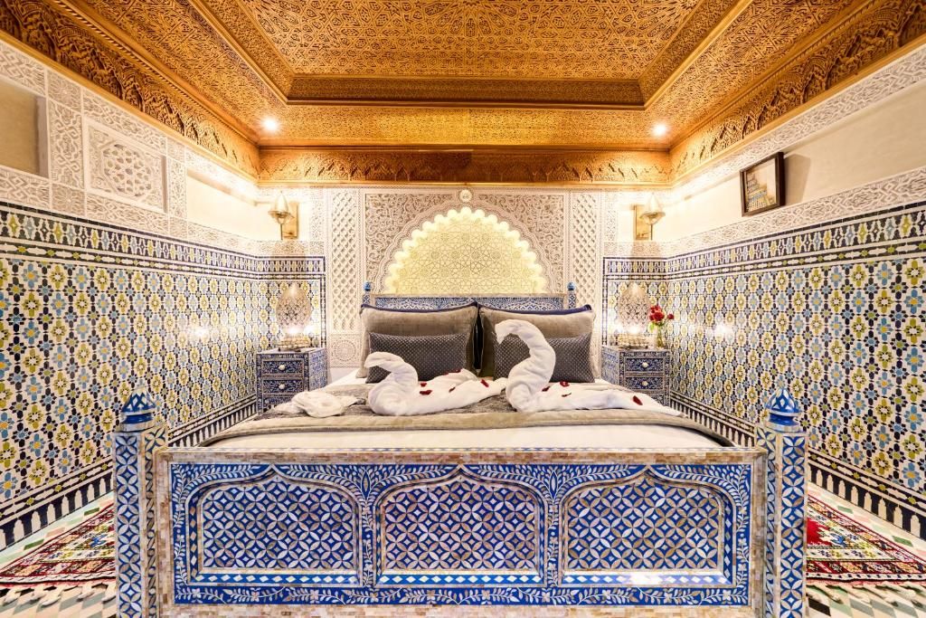 Quarto com cama grande, detalhes em azulejos elaborados e teto decorativo.