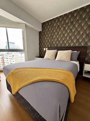 Quarto moderno com uma cama grande, parede estampada e vista para a cidade.