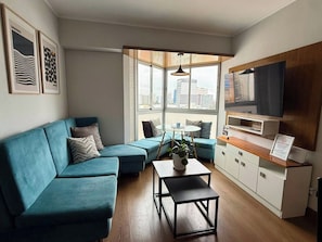 Uma sala de estar moderna com um sofá verde-turquesa, uma mesinha de centro e uma TV fixada na parede.