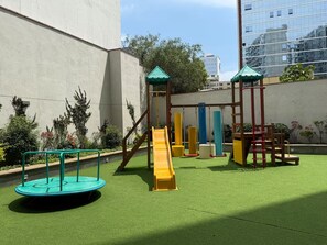 Uma área de recreação com escorrega, balanços e estrutura de escalada.