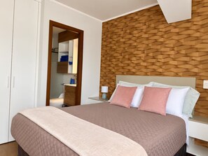Quarto com cama, mesa de cabeceira, espelho e parede com textura de madeira.