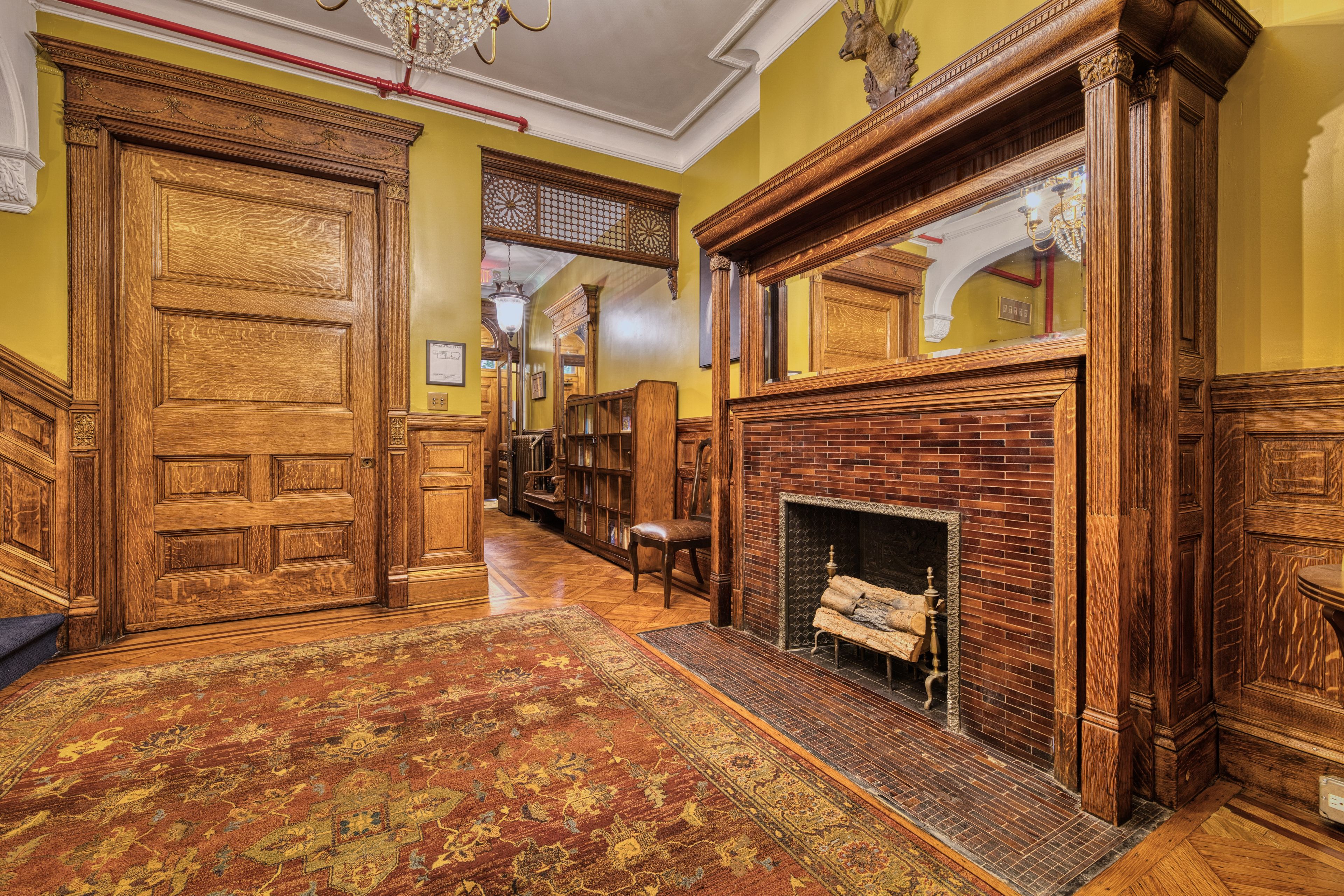 Interior de biblioteca tradicional, com estantes de madeira, lareira e uma grande porta de madeira.