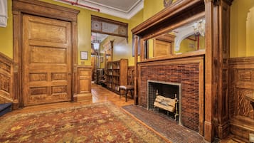 Interior de biblioteca tradicional, com estantes de madeira, lareira e uma grande porta de madeira.