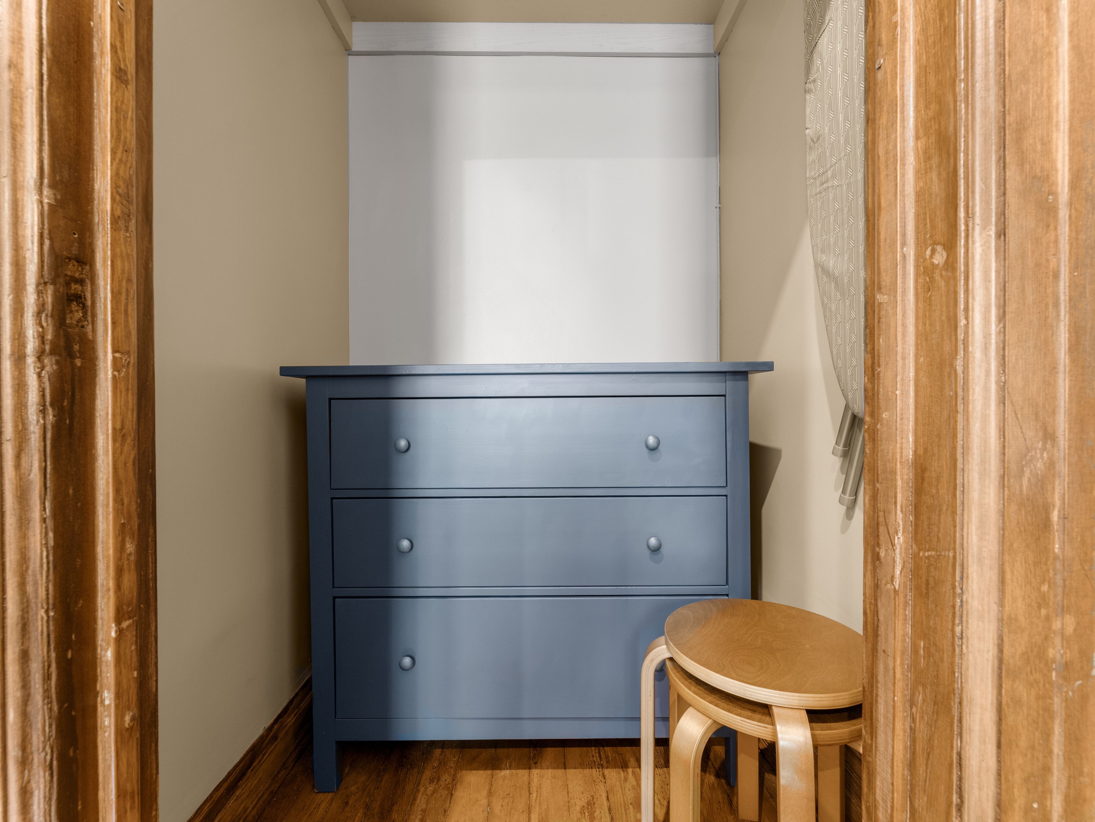 Um quarto pequeno com cômoda azul, cadeira de madeira e armário branco.