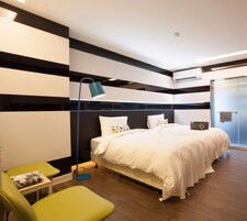 Quarto de hotel moderno com uma cama grande, uma mesinha de cabeceira, um abajur e uma cadeira verde.