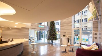 Um hall de hotel moderno com uma recepção, uma árvore de Natal e vista para a cidade.