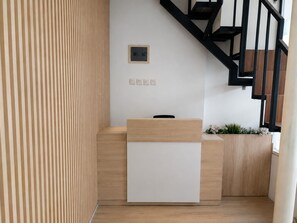 Balcão de recepção com design moderno, escada com corrimão preto e interruptor de luz fixado na parede.
