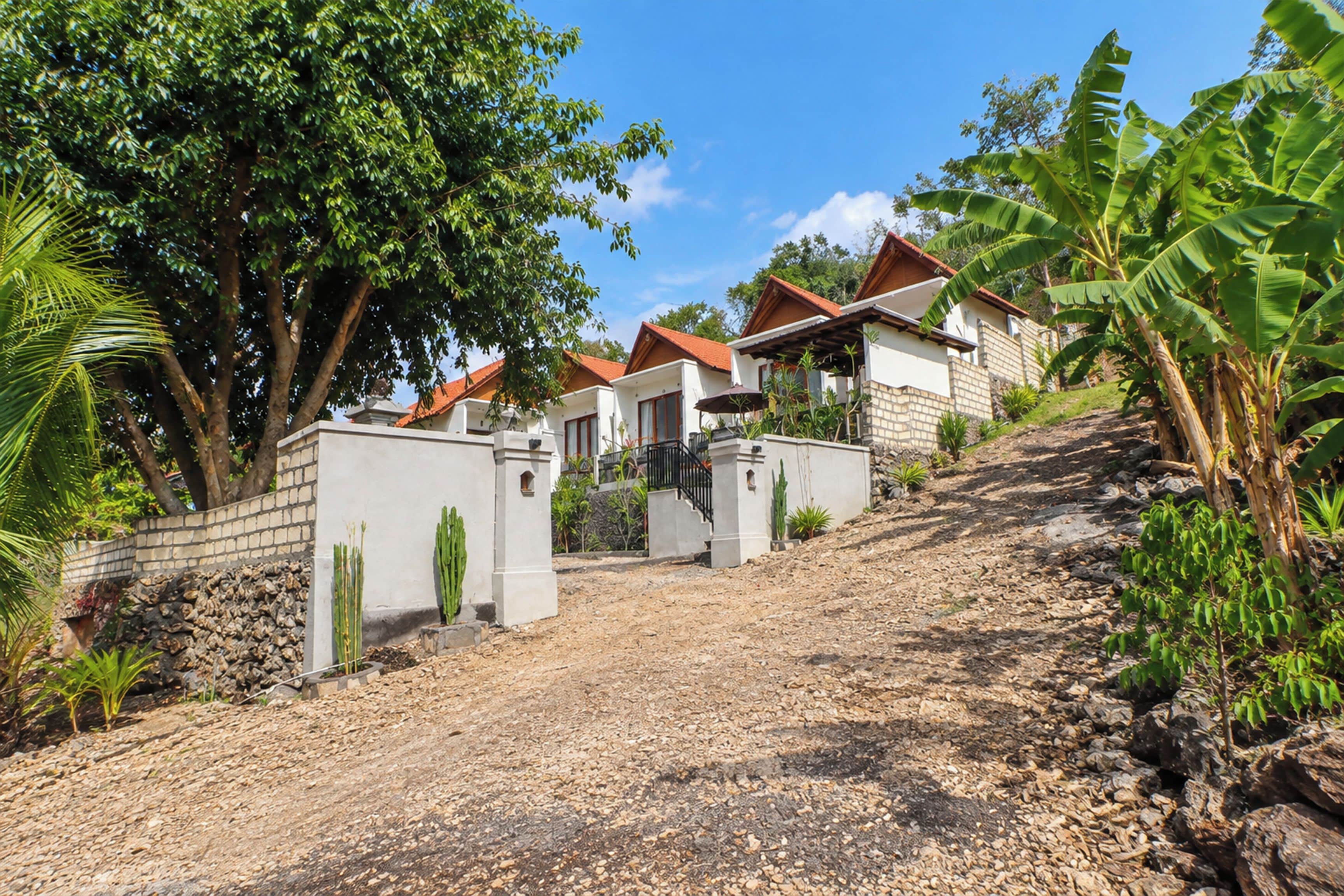 Imóvel residencial com calçada pavimentada que leva a um portão, cercado por vegetação exuberante e uma paisagem acidentada.