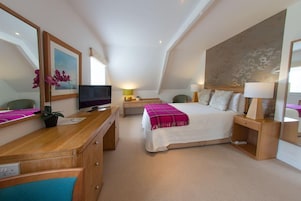 Quarto de hotel com cama, escrivaninha, televisão e uma janela grande.
