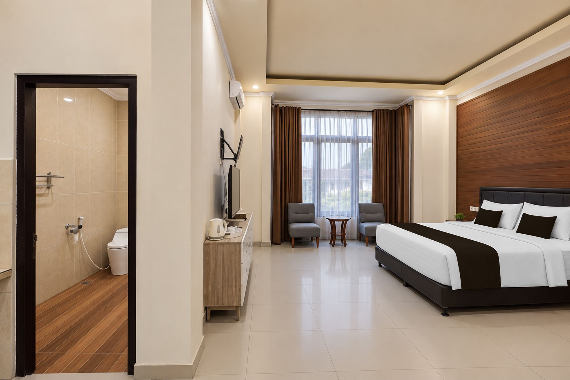 Quarto de hotel com cama, duas cadeiras, escrivaninha com computador, janela com cortinas e chuveiro.
