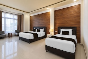 Quarto de hotel com duas camas, área de estar e uma janela grande com cortinas.
