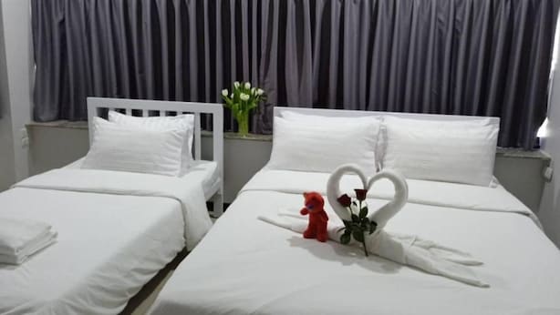 Quarto de hotel com duas camas, uma janela grande com cortinas, um vaso com flores e um urso de pelúcia em uma das camas.