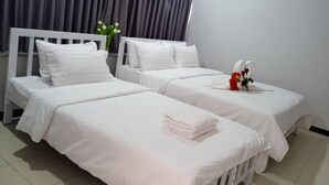 Quarto de hotel com duas camas de solteiro, roupa de cama branca, uma mesa pequena com um vaso de flores e uma cortina.