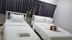 Quarto de hotel com duas camas de solteiro, uma mesa pequena com um vaso de flores e uma janela com cortinas.