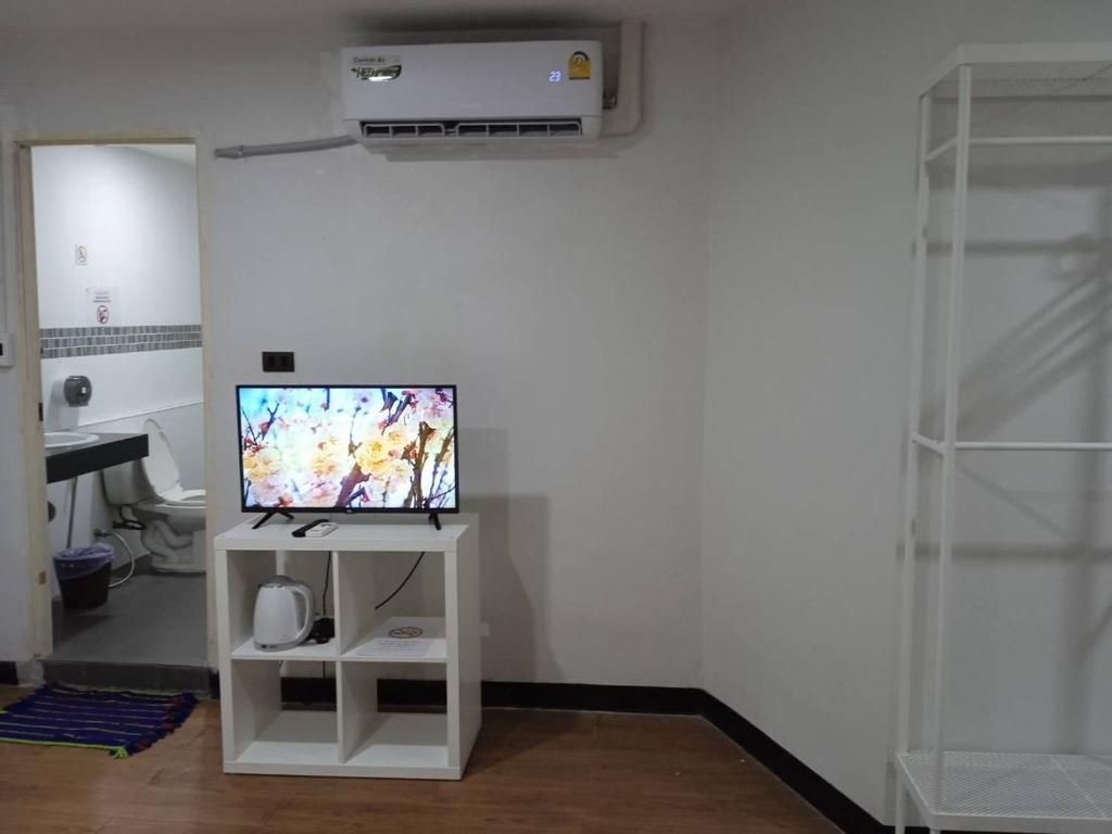 Quarto com estante branca, televisão, aparelho de ar condicionado e prateleira metálica branca.