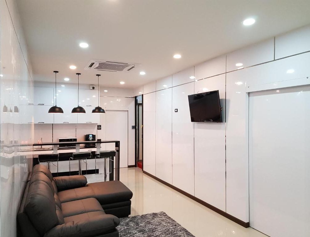 Uma sala de estar moderna com sofá, TV de tela plana fixada na parede e área de cozinha com mesa e cadeiras.