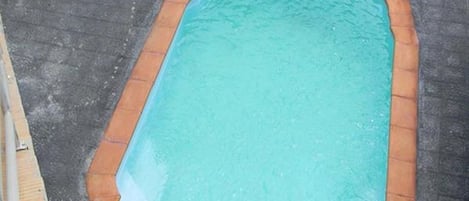 Piscina ao ar livre com borda azulejada, rodeada por espreguiçadeiras e um vaso de planta.