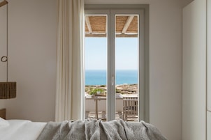 Quarto com uma grande porta de vidro deslizante que dá para uma varanda com vista para o mar.
