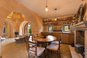 Uma cozinha espaçosa com uma mesa redonda de madeira, cadeiras e uma lareira de pedra.