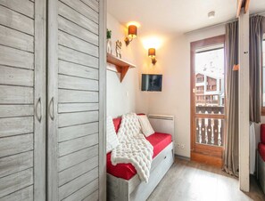 Quarto com cama, televisão e porta deslizante para uma varanda externa.