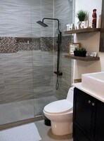 Um banheiro moderno com box de vidro, vaso sanitário branco e armário preto.