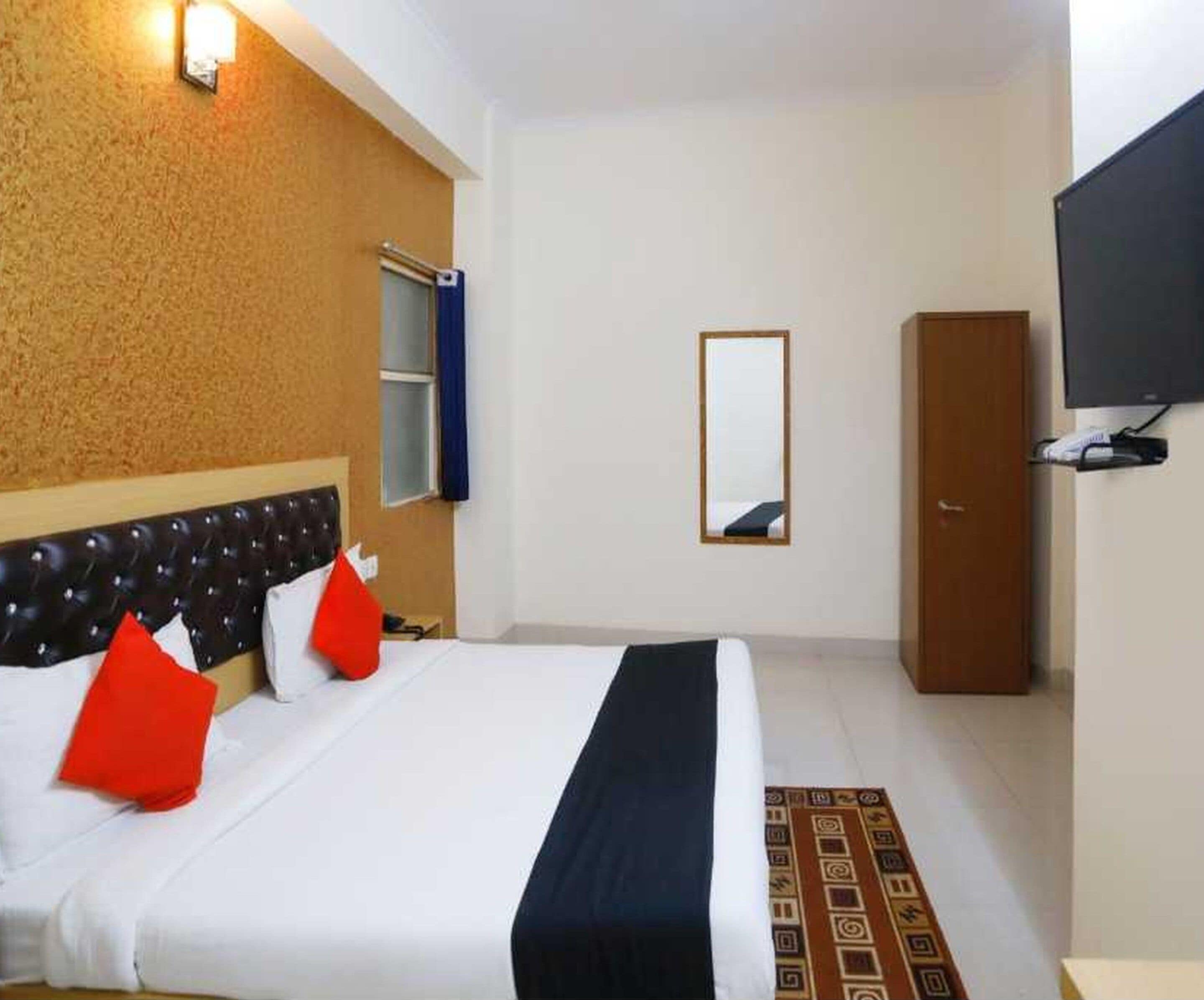 Quarto de hotel com cama, guarda-roupa, televisão e espelho.