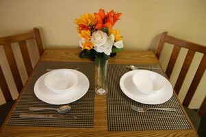 Uma mesa de jantar posta com pratos brancos, um vaso de vidro transparente com flores e um jogo americano tecido.