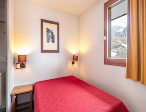 Quarto com cama, duas luminárias na parede, um quadro e janela com vista para uma paisagem montanhosa.