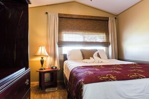 Quarto de hotel com cama, mesa de cabeceira, abajur e janela com cortinas.