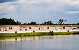 Uma fileira de edifícios térreos com telhado plano, possivelmente um hotel ou motel, localizada à beira de um corpo d'água com reflexo límpido.