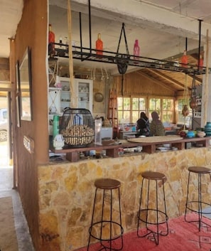 Um espaço de bar rústico com balcão de pedra, banquetas e decorações penduradas.