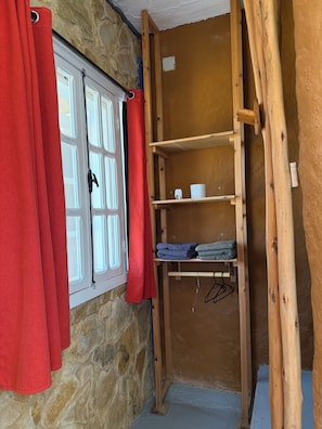 Quarto com parede de pedra, estante de madeira e janela com cortinas.