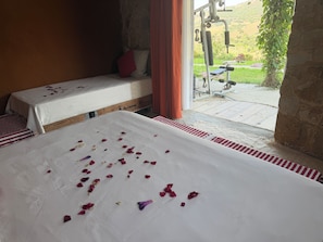 Quarto com duas camas, uma com travesseiro vermelho e outra com travesseiro branco. Pétalas de rosa espalhadas sobre as camas.