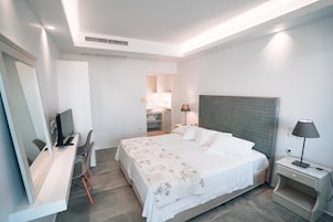 Quarto de hotel com cama, escrivaninha com computador, cadeira, mesa de cabeceira com abajur e guarda-roupa.